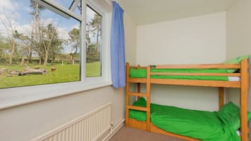 Um quarto com uma cama beliche, uma janela com vista para árvores e grama, e um radiador na parede.