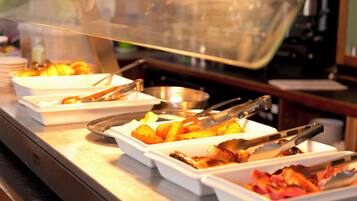 Buffet com diversos pratos em bandejas brancas, incluindo frituras e carnes grelhadas.