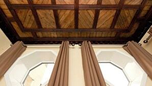 Quarto com teto de madeira e dois claraboias com cortinas castanhas.