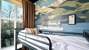 Uma cama beliche com um mural de um barco na parede, uma janela com cortinas e um certificado emoldurado na parede.