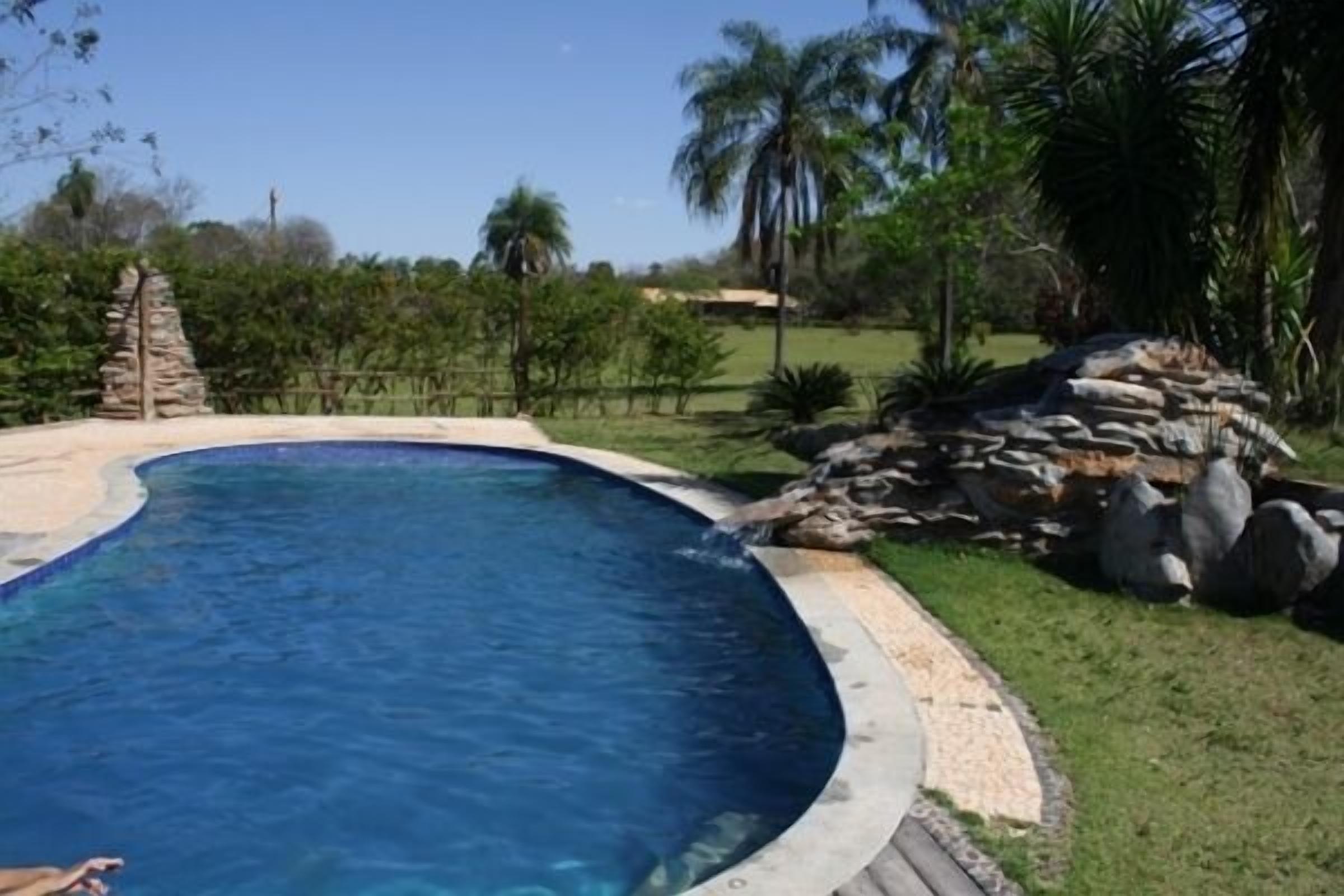 Piscina azul límpida rodeada por um muro de pedra e vegetação.