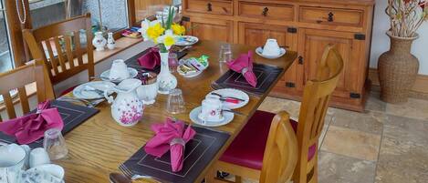 Uma sala de jantar com mesa de madeira posta para refeição, rodeada por cadeiras.