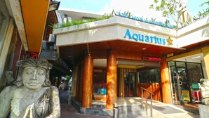 Exterior do Hotel Aquarius, com entrada destacada, um logotipo em forma de estrela, uma estátua de mulher e um letreiro anunciando quarto com preço especial.