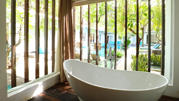 Uma banheira grande e independente em um quarto com vista para uma piscina e móveis de exterior.