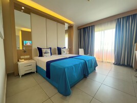 Quarto de hotel com uma cama grande, uma mesinha de cabeceira com telefone, um espelho e uma televisão.