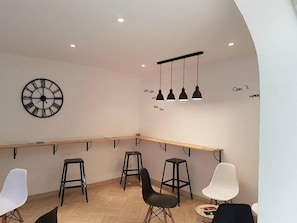 Um interior moderno com balcão de madeira, banquetas pretas, uma cadeira branca e um relógio de parede.