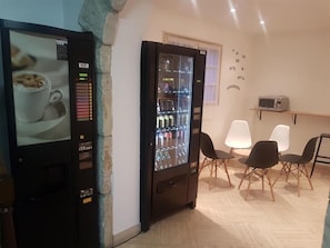 Quarto com máquina de vendas automática, micro-ondas e área de estar com cadeiras.
