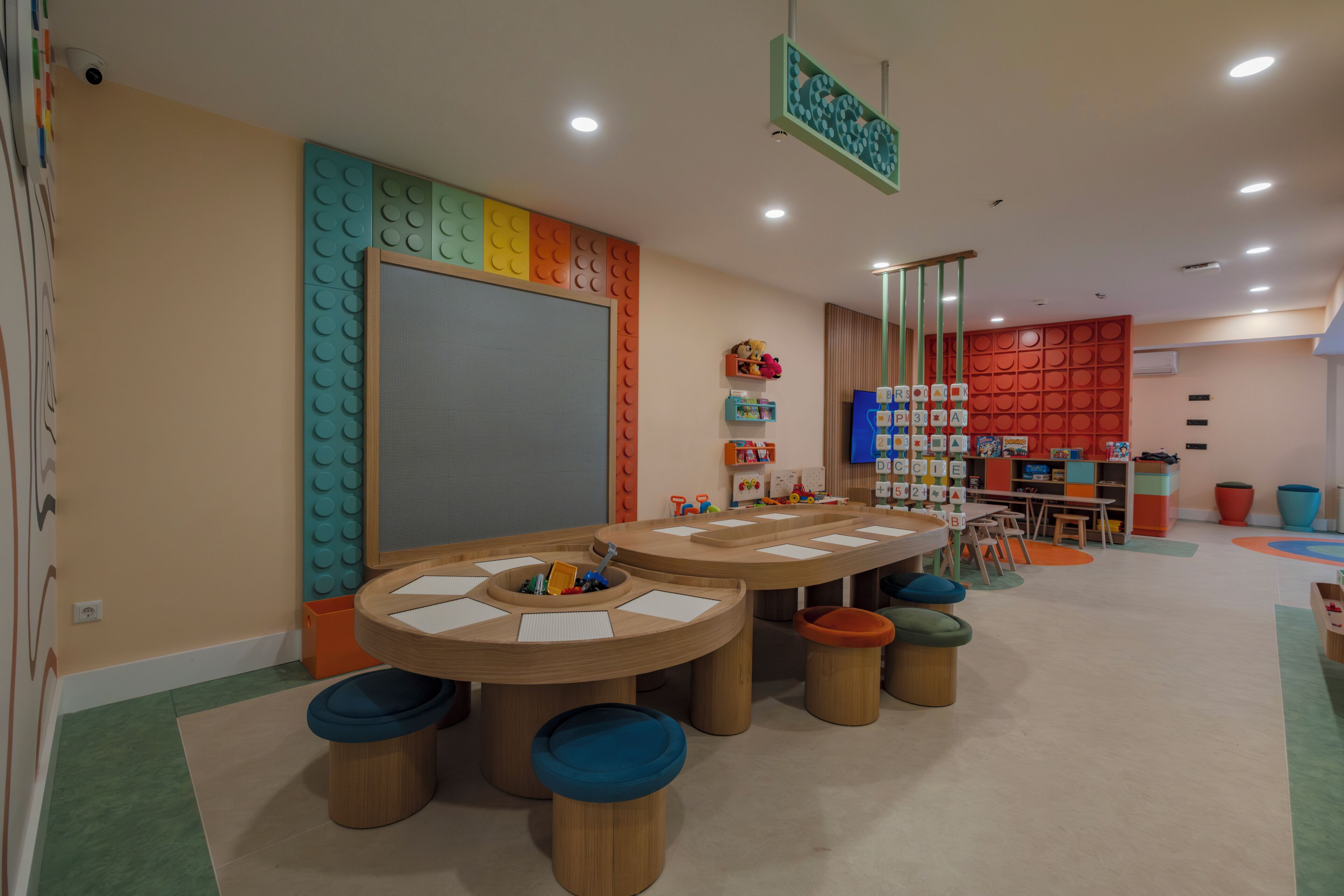 Uma sala de jogos infantil com mesas redondas, banquetas e brinquedos educativos.