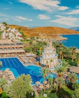 Um resort com uma piscina grande, uma torre de pedra circular e vista para o mar.