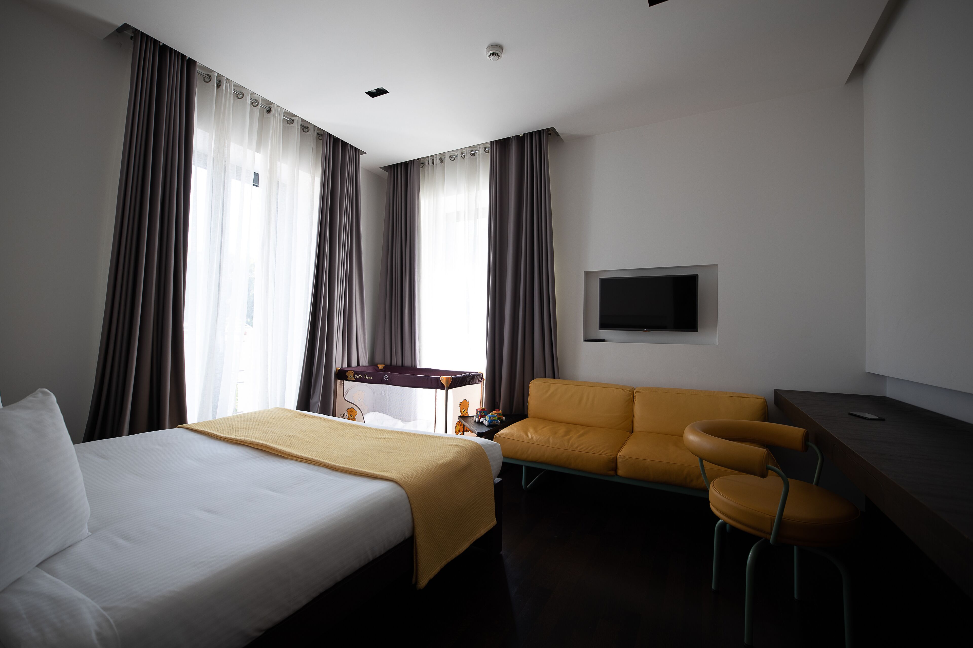 Quarto de hotel com cama, sofá, escrivaninha e televisão.