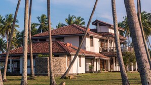 Uma casa de vários andares com telhado de telhas, rodeada por palmeiras.