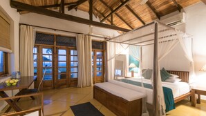 Quarto com cama, escrivaninha, cadeira e vista para o mar.