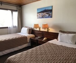Quarto de hotel com duas camas, mesa de cabeceira, luminária, pintura e janela com cortinas.