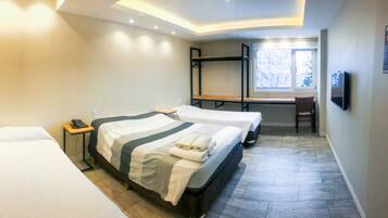 Quarto de hotel com duas camas, uma escrivaninha e uma cadeira.