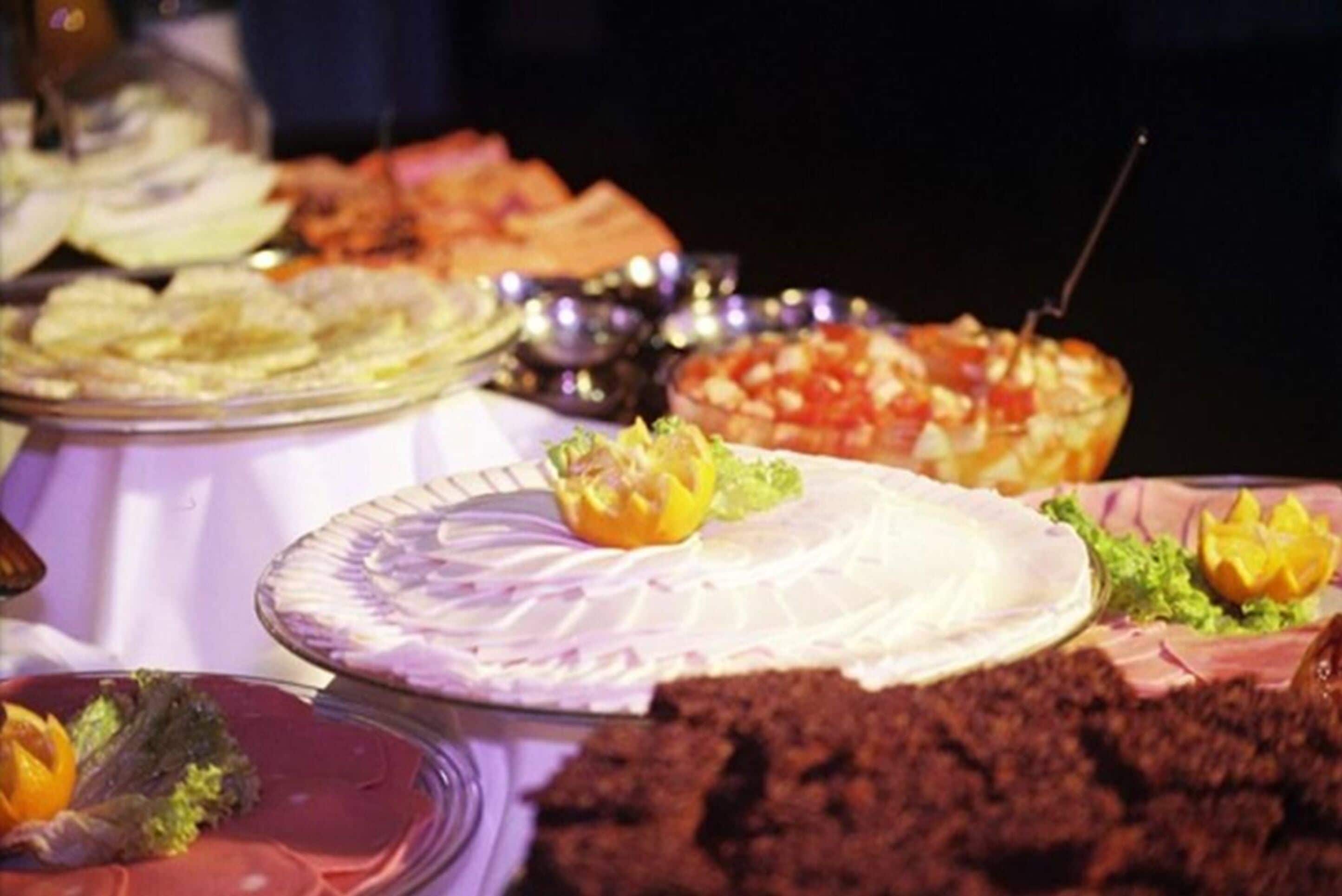 Mesa de buffet com diversos pratos, incluindo bolo, saladas e uma saladeira de frutas.