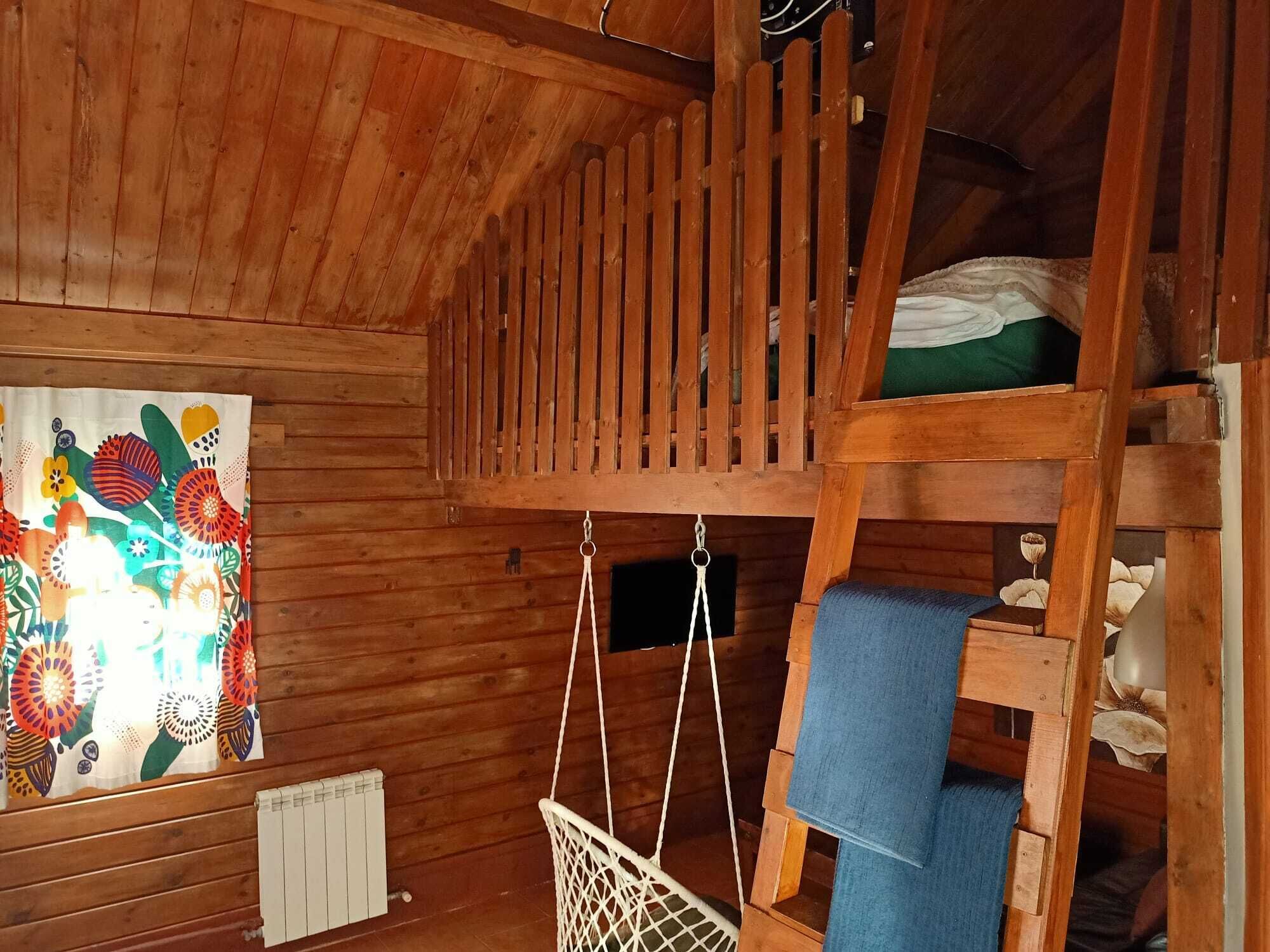 Interior de cabana de madeira com uma beliche, uma rede e uma obra de arte colorida na parede.