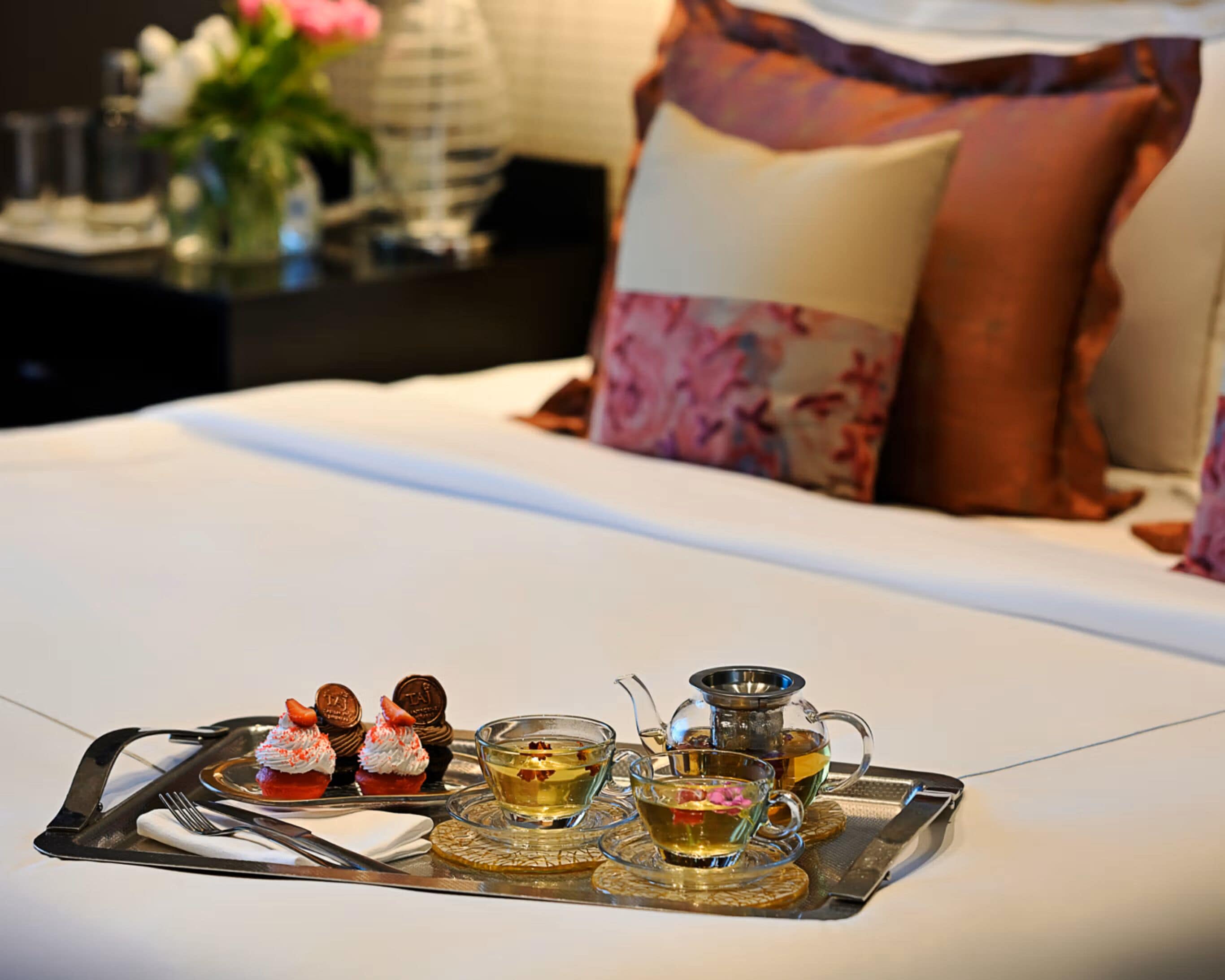 Uma bandeja com sobremesas e chá sobre uma cama de hotel.