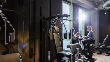 Uma academia com equipamentos de ginástica, esteira e janela com luz natural.