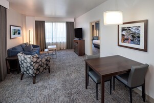 Quarto de hotel com sofá, mesa de jantar, televisão, escrivaninha e cama.