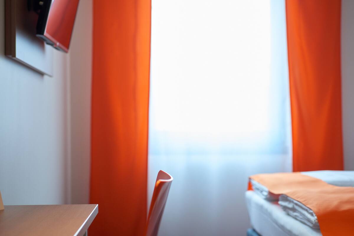 Quarto de hotel com cama, cortinas laranja e uma janela.