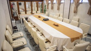 Uma sala de conferências com uma mesa comprida, cadeiras bege e um projetor.