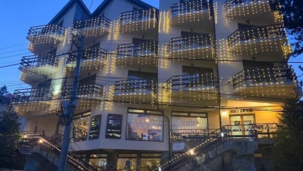 Um hotel de vários andares com varandas decoradas com luzes de cordão, área de recepção e escadaria que leva à entrada.