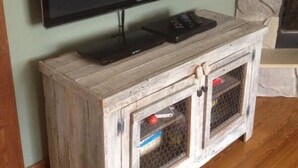 Uma televisão fixada em um armário rústico de madeira com duas portas de vidro, localizada em um quarto com lareira de pedra.