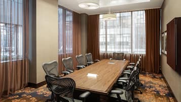 Uma sala de conferências com uma mesa comprida, cadeiras e janelas amplas com cortinas.