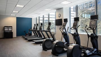 Uma academia com esteiras, elípticos e uma TV fixada na parede.