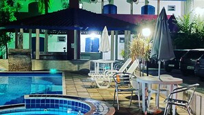 Uma área de piscina ao ar livre com hidromassagem, espreguiçadeiras e guarda-sóis.