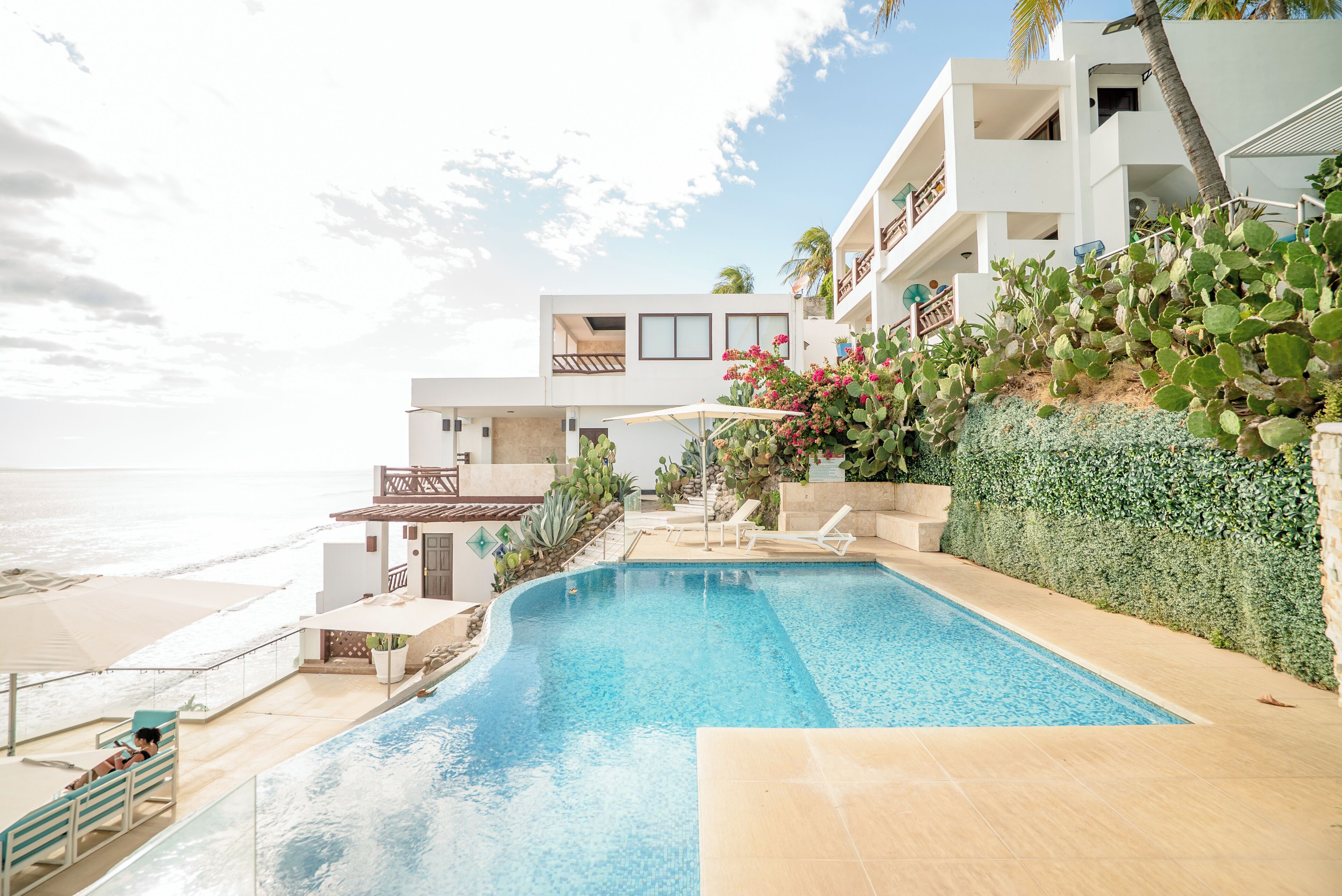 Um hotel moderno com piscina, vista para a praia e um muro verde exuberante.