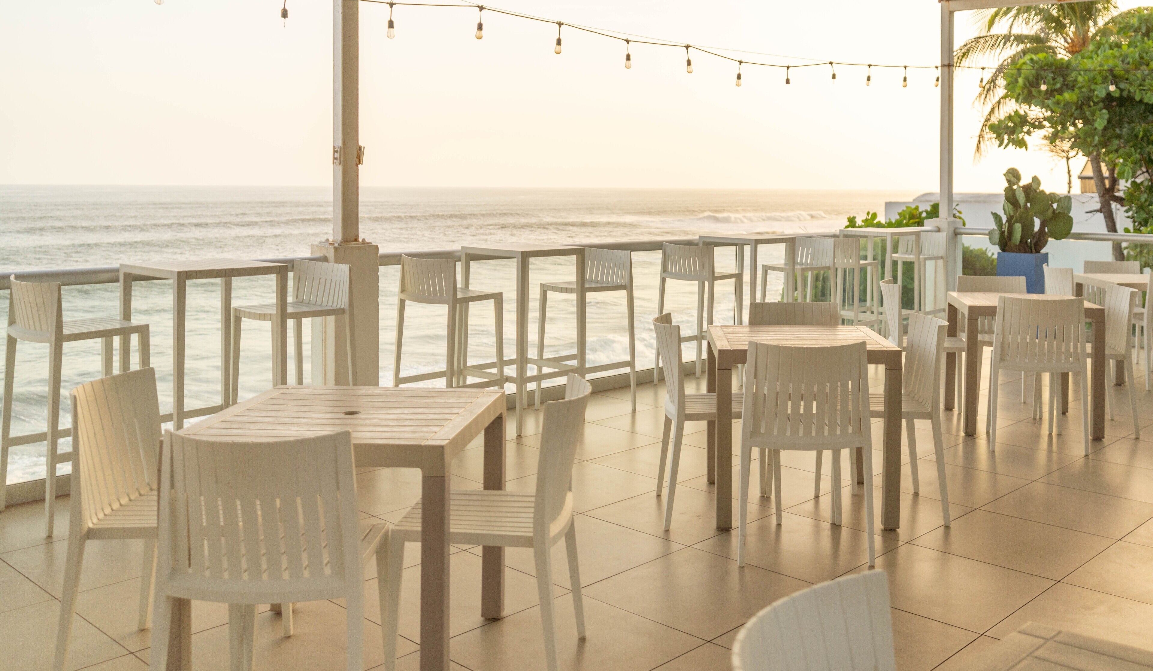 Um restaurante à beira-mar com mesas ao ar livre, vista para o oceano e luzes de festa.
