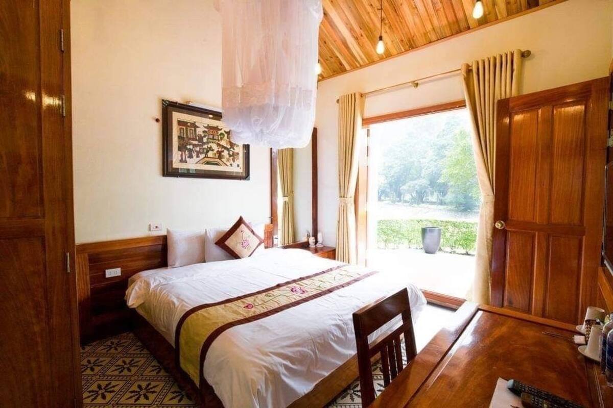 Quarto com cama, escrivaninha, cadeira, mosquiteiro suspenso, quadro na parede e janela com cortinas.