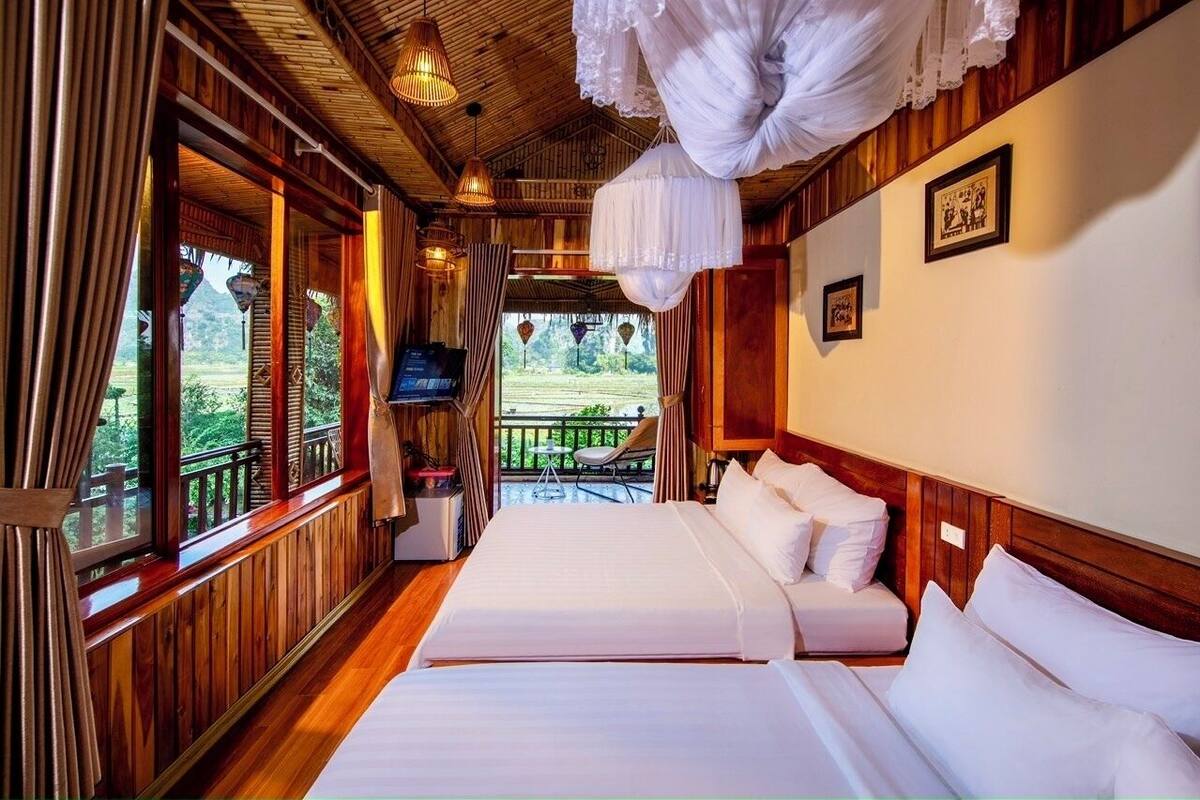Quarto acolhedor com teto de madeira, cama grande, varanda com vista para vegetação e um dossel branco suspenso.