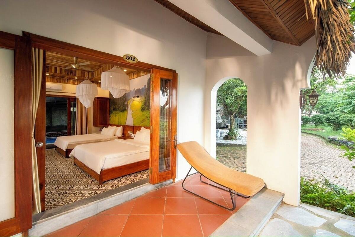 Quarto de hotel com duas camas, área de estar e vista para um jardim.