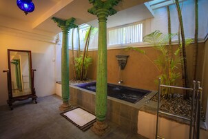 Um banheiro com banheira, colunas, espelho e plantas.