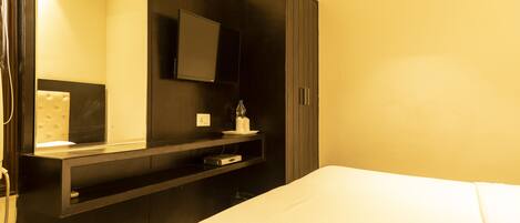 Quarto de hotel com uma cama, televisão fixada na parede, mesa de cabeceira e guarda-roupa.