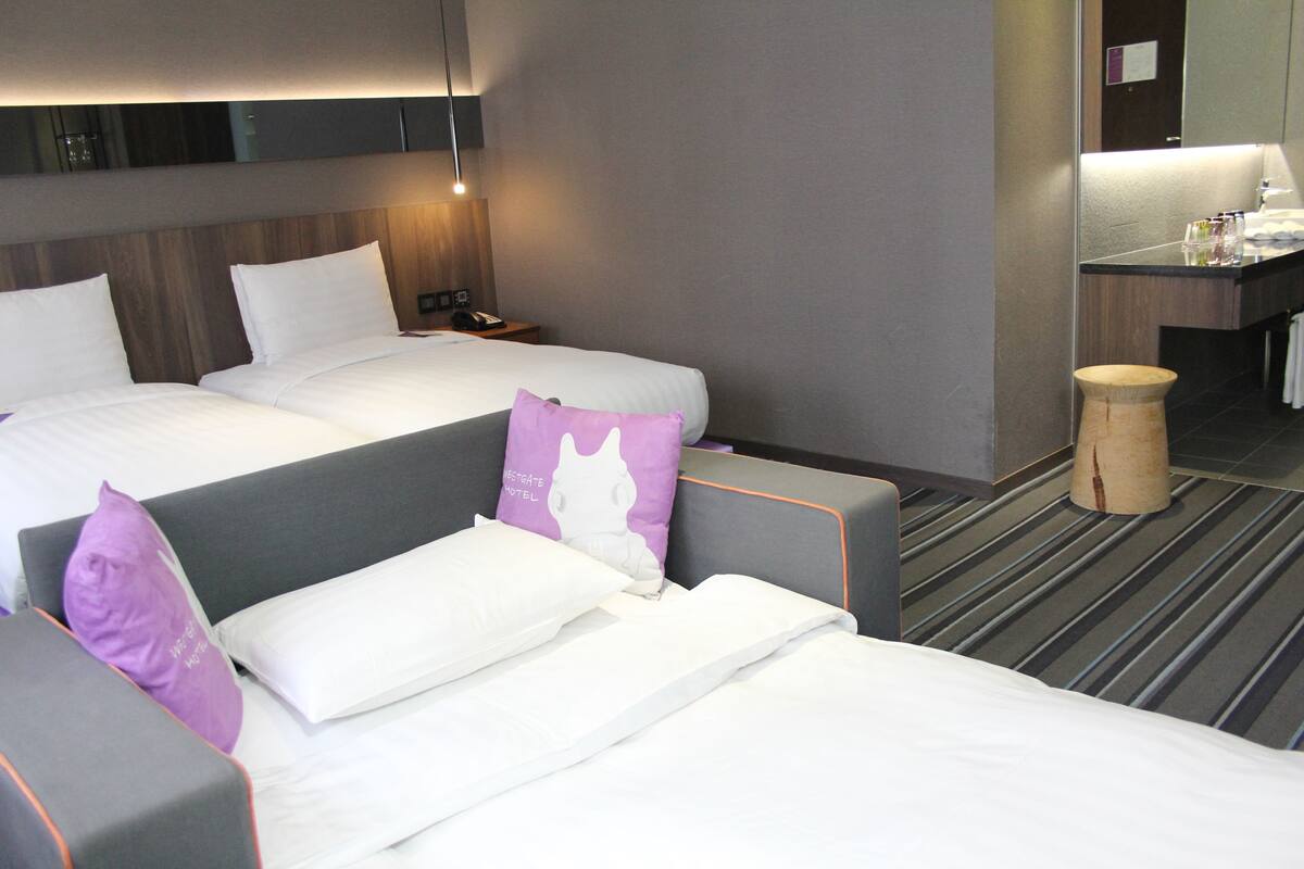 Quarto de hotel com duas camas, uma pequena mesa e um espelho.