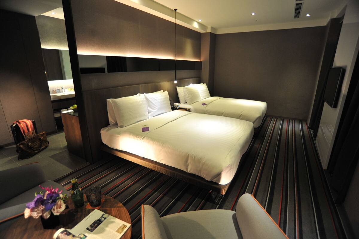 Quarto de hotel com duas camas, uma mesinha com um vaso de flores, uma cadeira e um frigobar.
