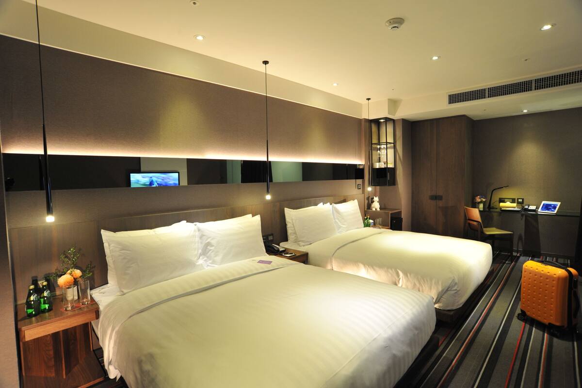 Quarto de hotel com duas camas, uma escrivaninha com computador e um pequeno espaço de estar.