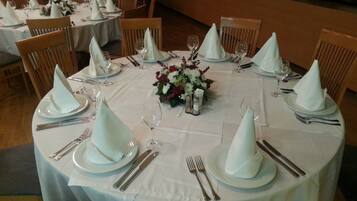 Mesa de jantar redonda posta para uma refeição formal, com toalhas brancas, talheres e guardanapos dobrados.