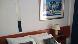 Quarto de hotel com uma cama grande, duas almofadas, mesa de cabeceira com abajur e um quadro na parede.