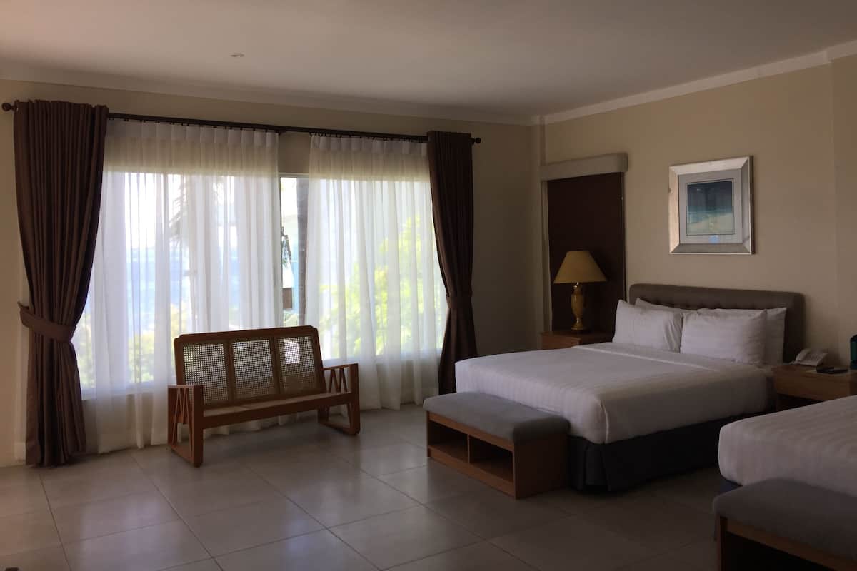 Quarto de hotel com duas camas, um banquinho de madeira, uma luminária e um quadro na parede.