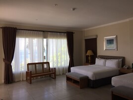 Quarto de hotel com duas camas, um banquinho de madeira, uma luminária e um quadro na parede.