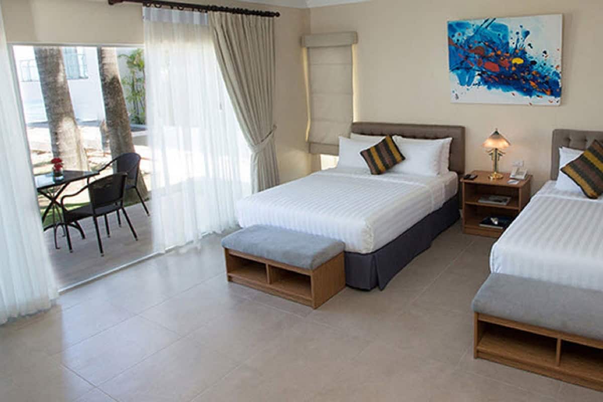Quarto de hotel com duas camas, uma mesinha, uma cadeira e vista para o exterior.