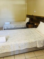 Duas camas de solteiro com roupa de cama estampada, uma mesinha de cabeceira com abajur e um telefone fixo na parede.