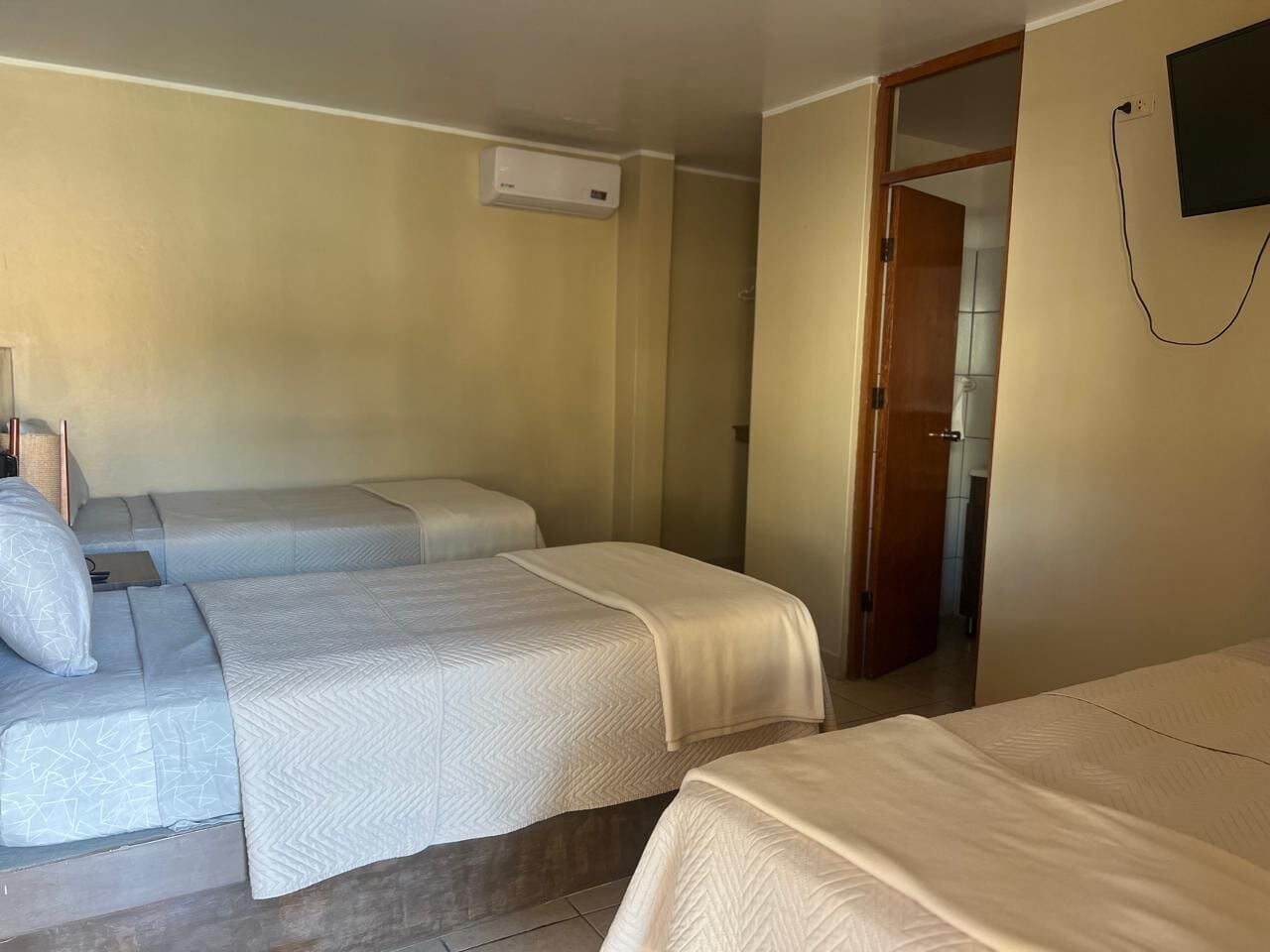 Quarto de hotel com duas camas, uma TV de tela plana na parede e um aparelho de ar condicionado.