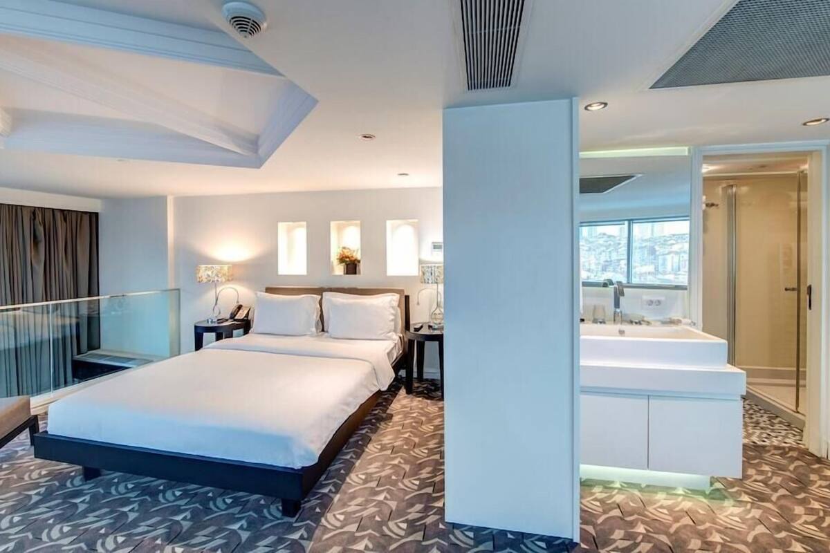 Quarto de hotel com uma cama grande, área de estar, banheiro com banheira e vista para a cidade.