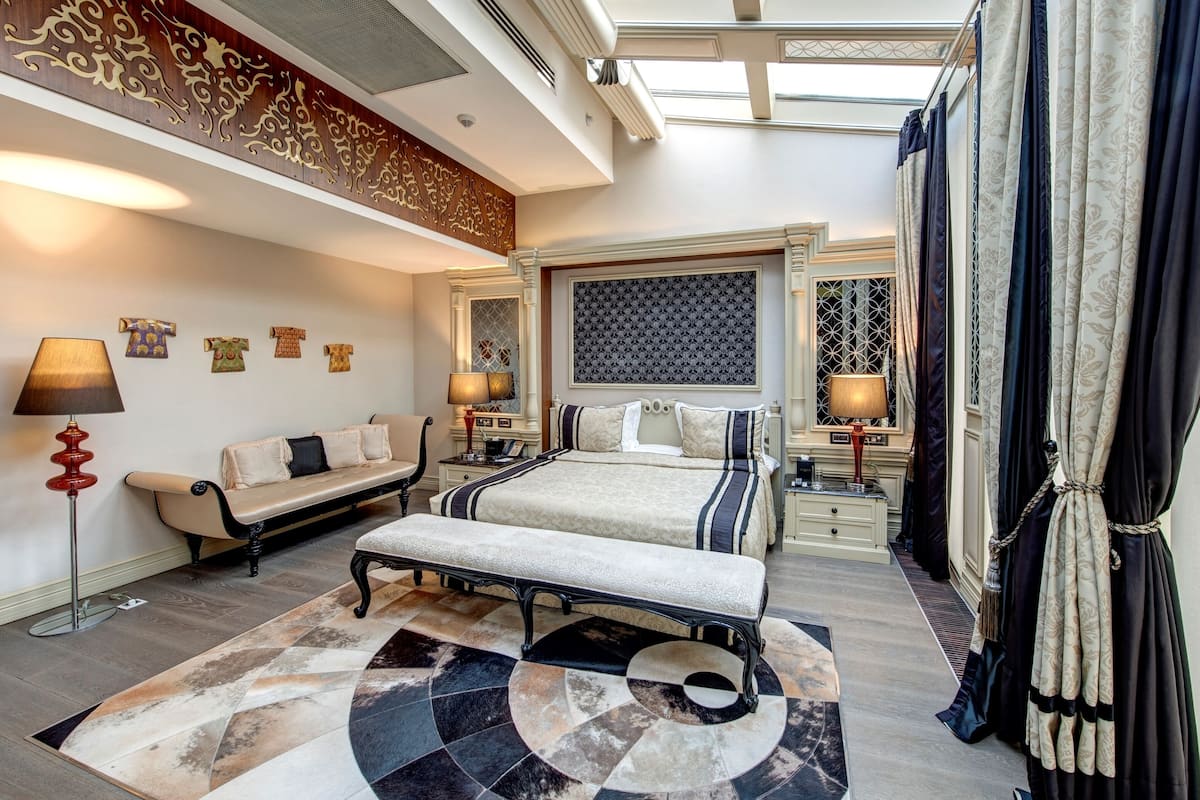 Um quarto espaçoso com uma cama grande, um banco, um sofá e uma mesa de cabeceira com abajures.