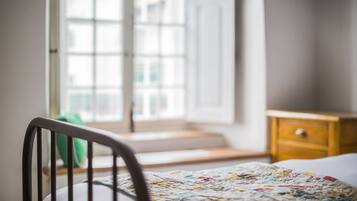 Quarto com cama, mesa de cabeceira de madeira e janela com vista para o exterior.